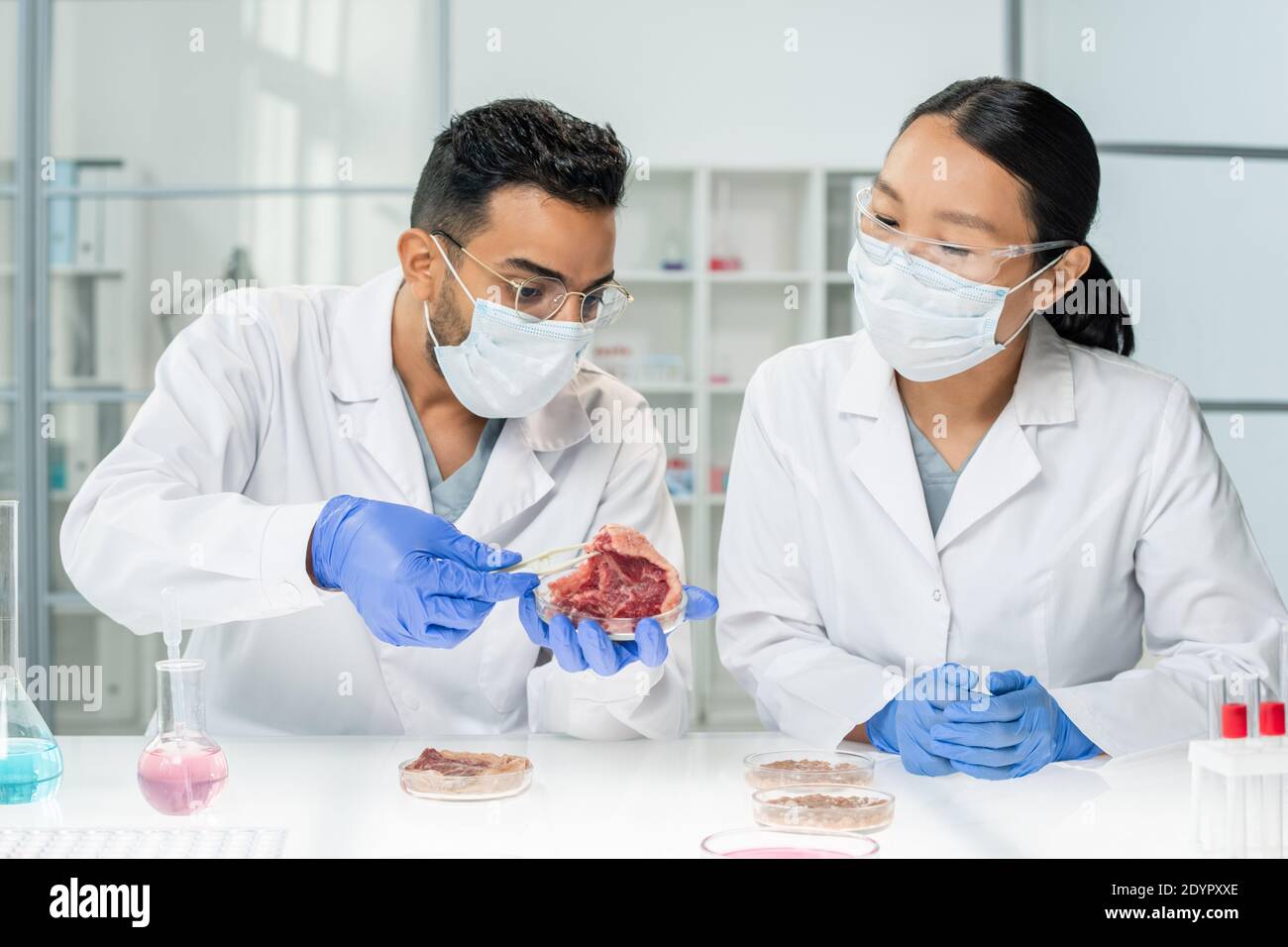 Two young researchers or clinicians in whitecoats, protective masks and ...