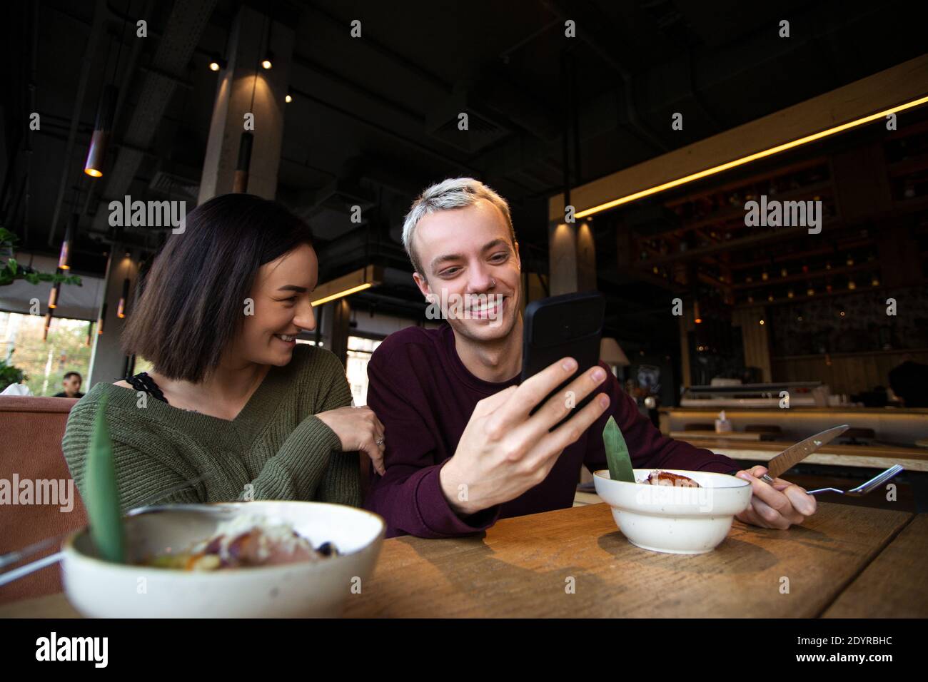 Couple eating in restaurant and laughing. Man showing memes to woman ...