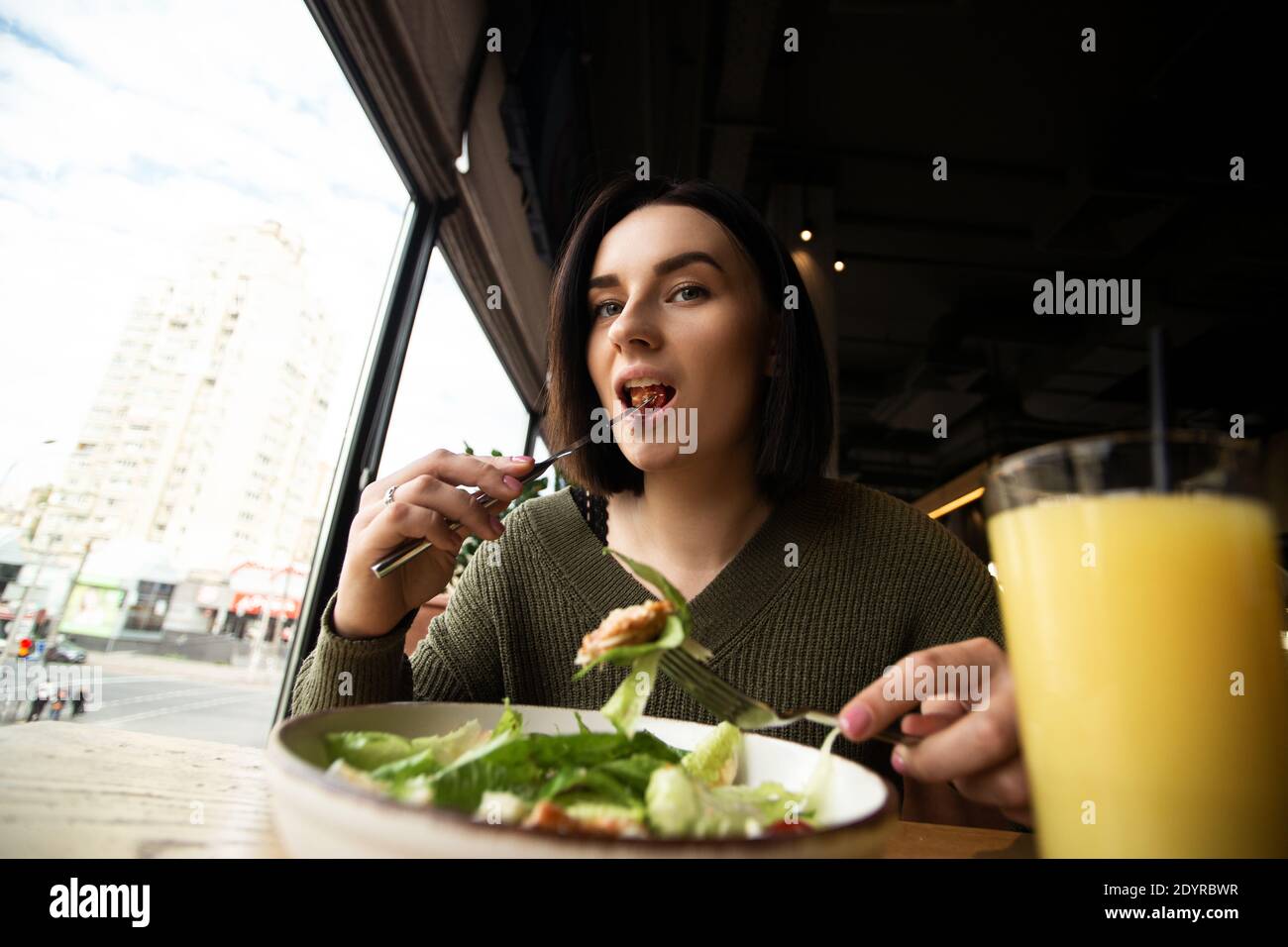Brunette woman eating caesar salad with pleasure. Blurred glass of ...