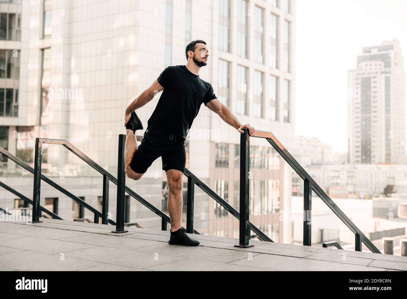 Athletic Man Stretching Legs Before Workout Outdoors Runner In Black