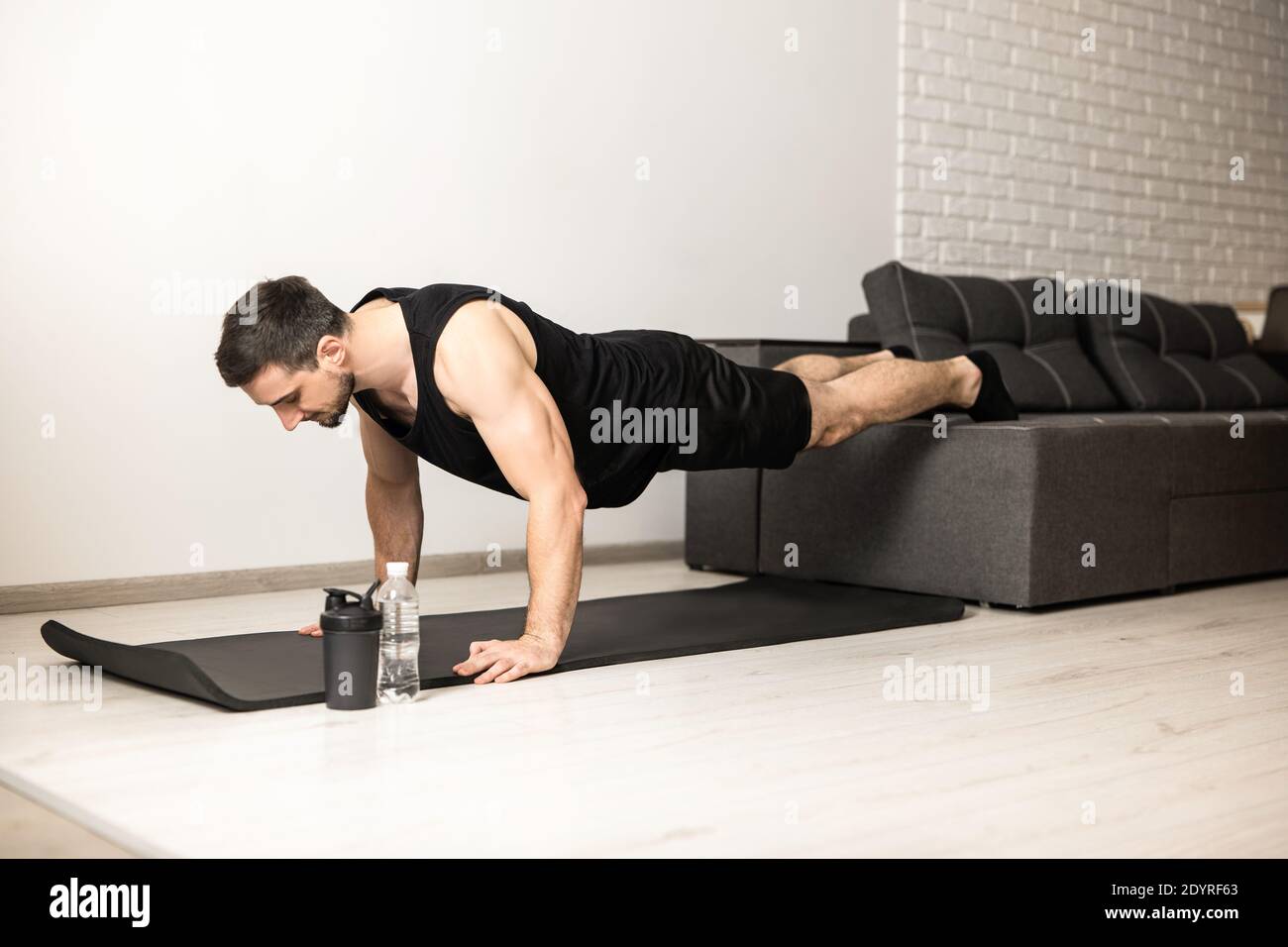 Sporty man pushing from floor with legs on sofa. Workout on black yoga ...
