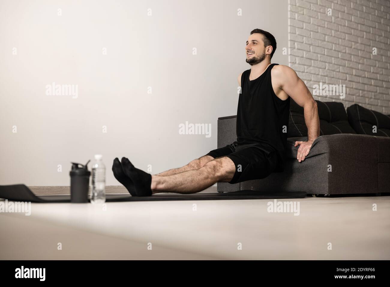 Attractive man pushing from sofa. Black sportswear. Man practicing hard ...