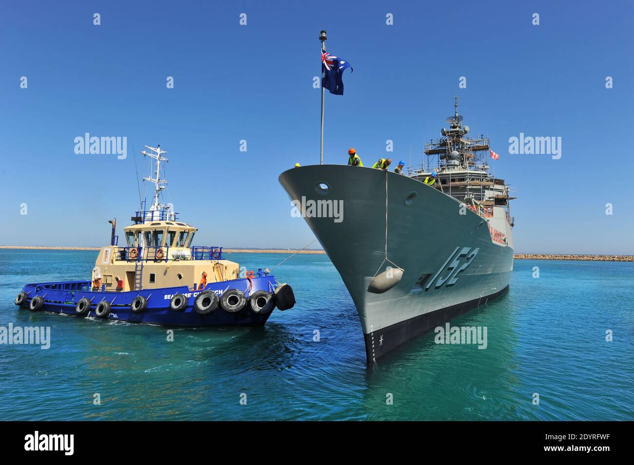 An Australian navy Frigate being helped into its berth by a harbour tug ...