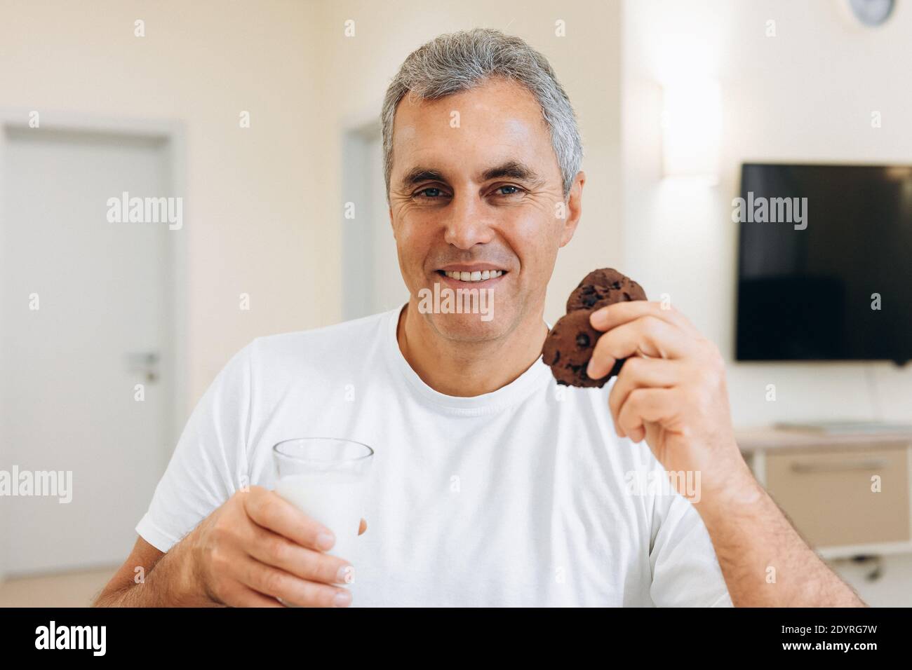 Adult man eating cookies and drinking milk. Modern light room on ...