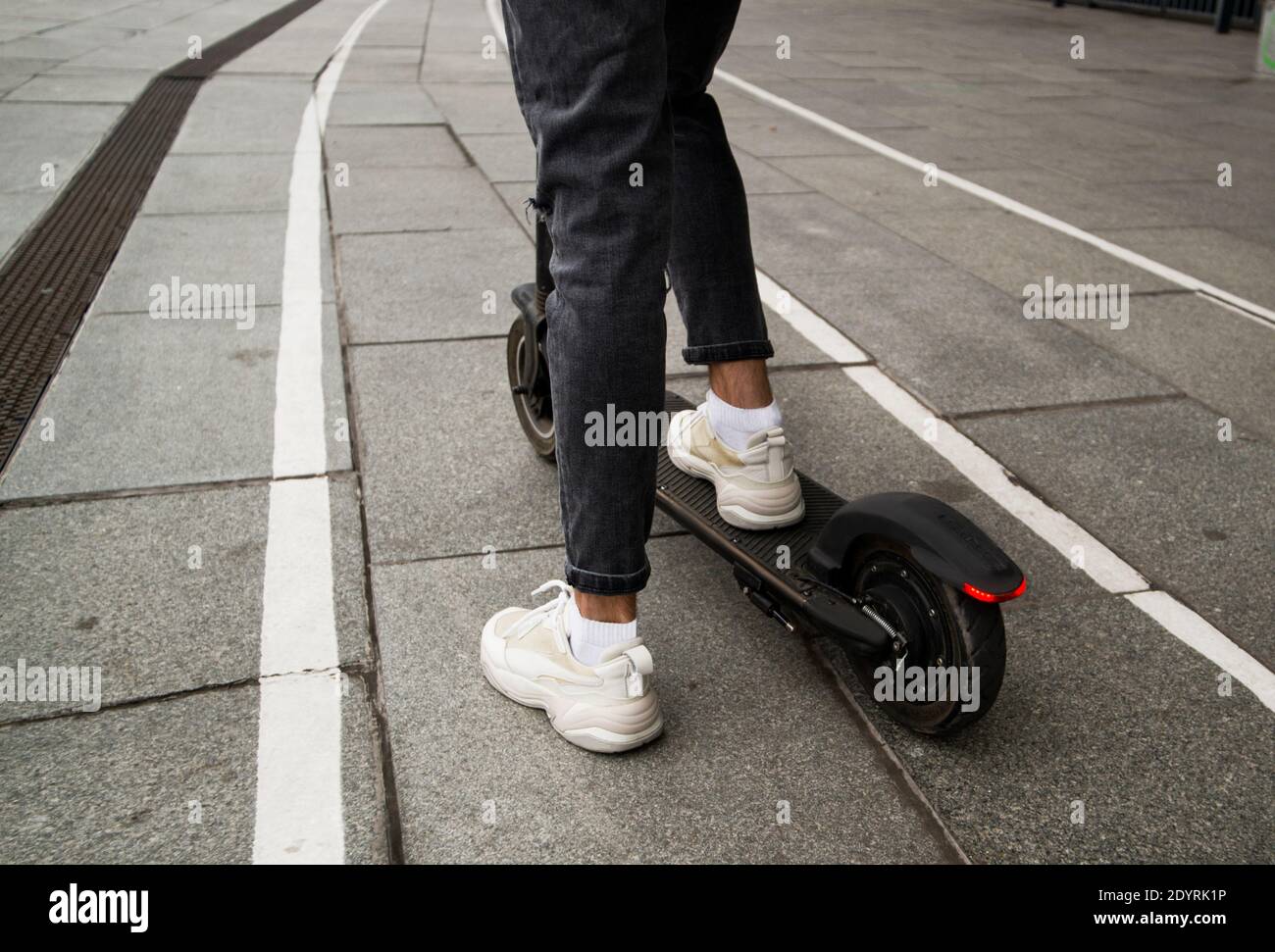 Legs of anonymous guy riding modern electric scooter on asphalt path on ...