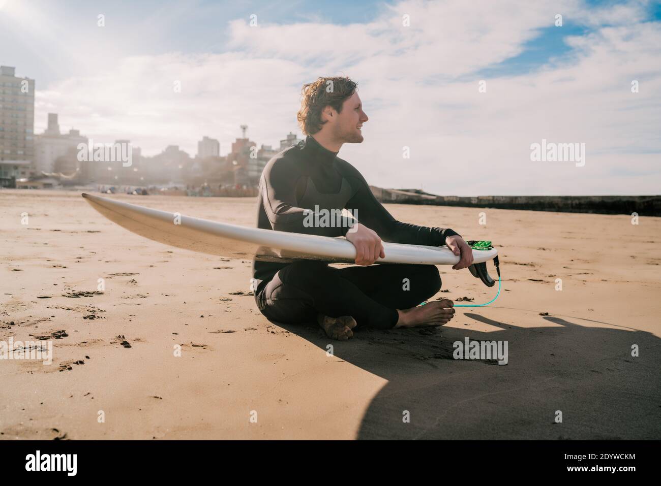 Surfer sitting on sandy beach with surfboard Stock Photo - Alamy