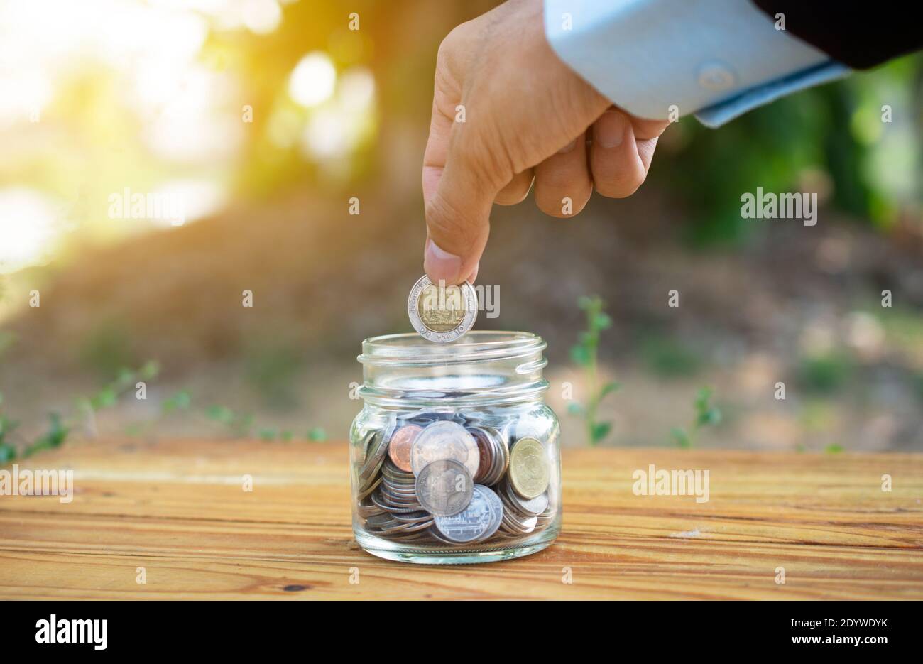 Hand putting coins in jar hi-res stock photography and images - Alamy