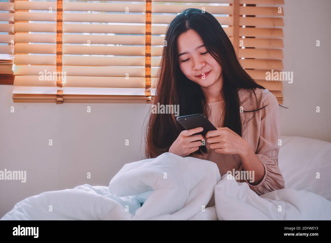 Women holding Mobile smartphone sitting on bed in room Stock Photo - Alamy