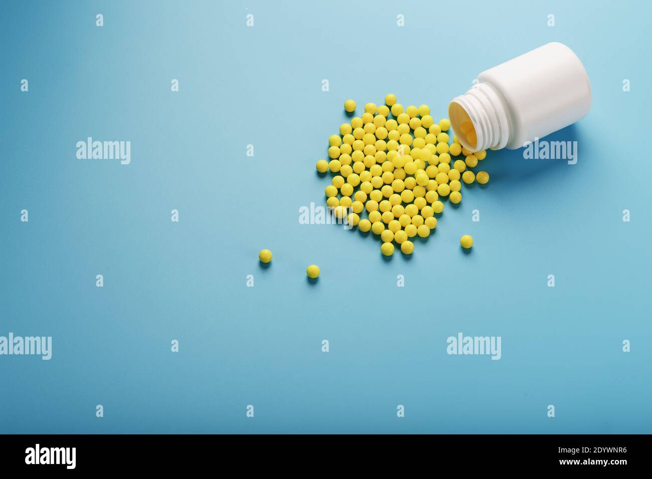 Yellow vitamin C capsules spilled out of a white jar against a blue ...