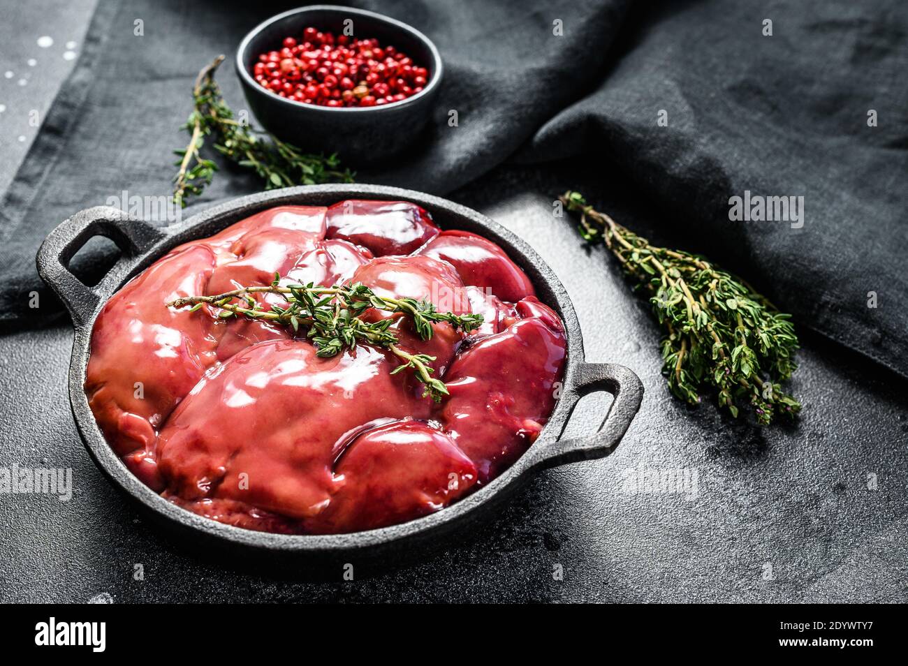 Raw Turkey liver in a frying pan. Black background. Top view. Copy ...