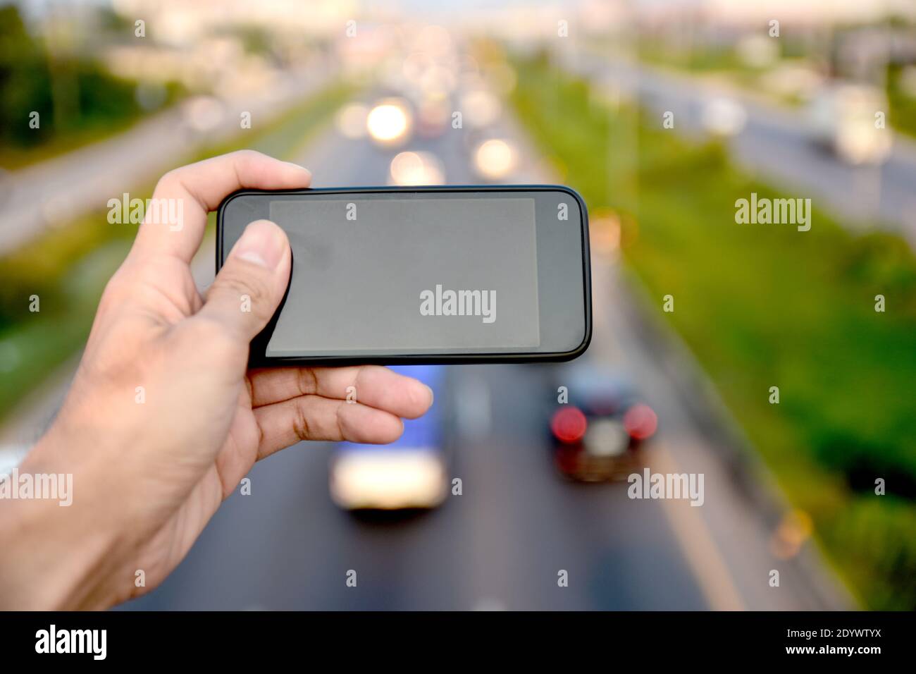 Hand holding smartphone against background many car driving on road ...