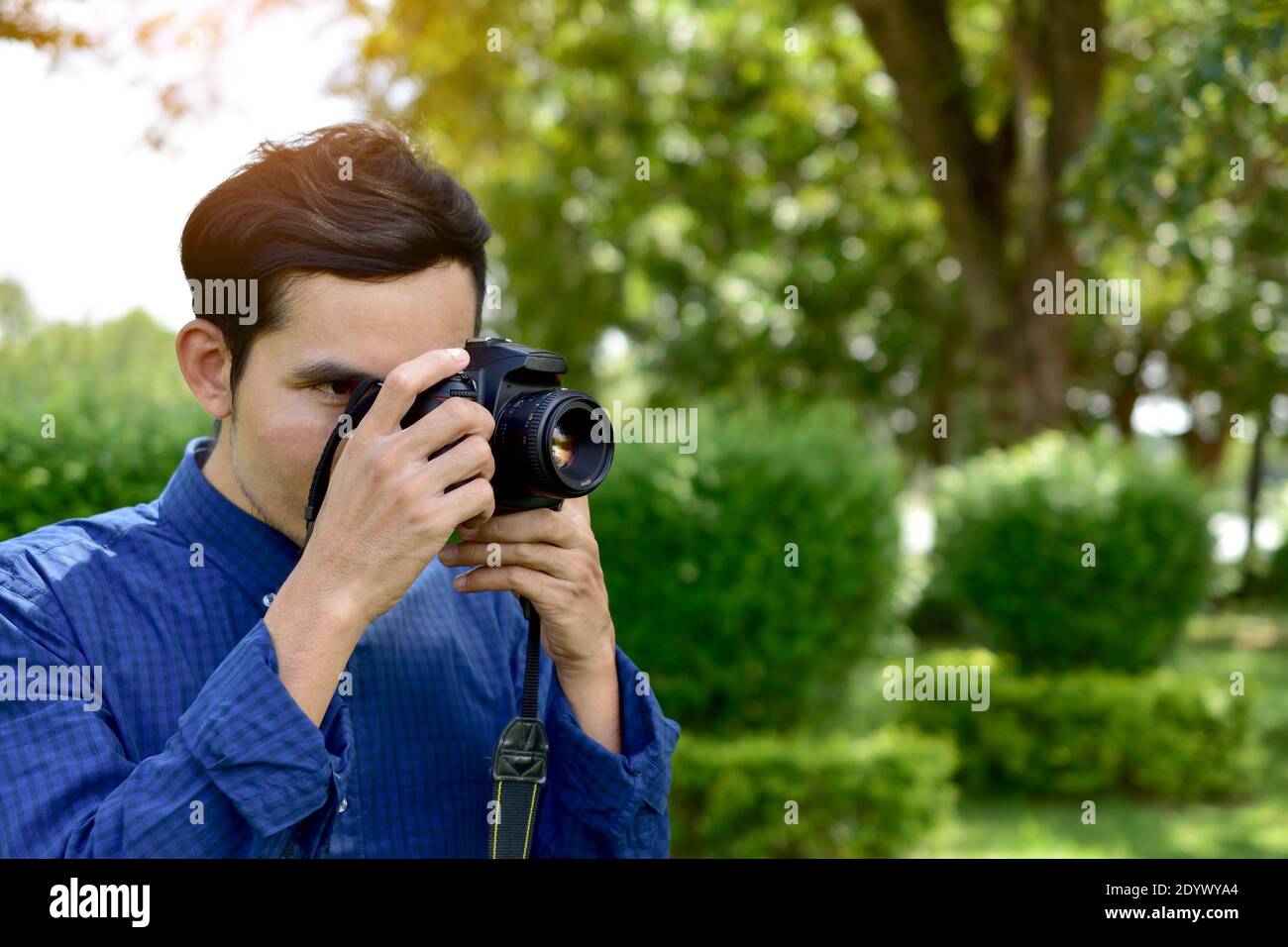 Man holding and using Dslr camera and sitting under tree in public park ...