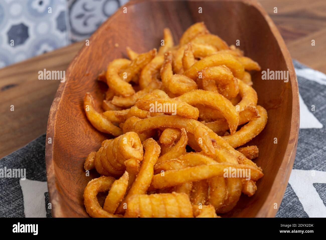 Curly fries, coated in herbs and spices, in a wooden dish bowl. Fast ...