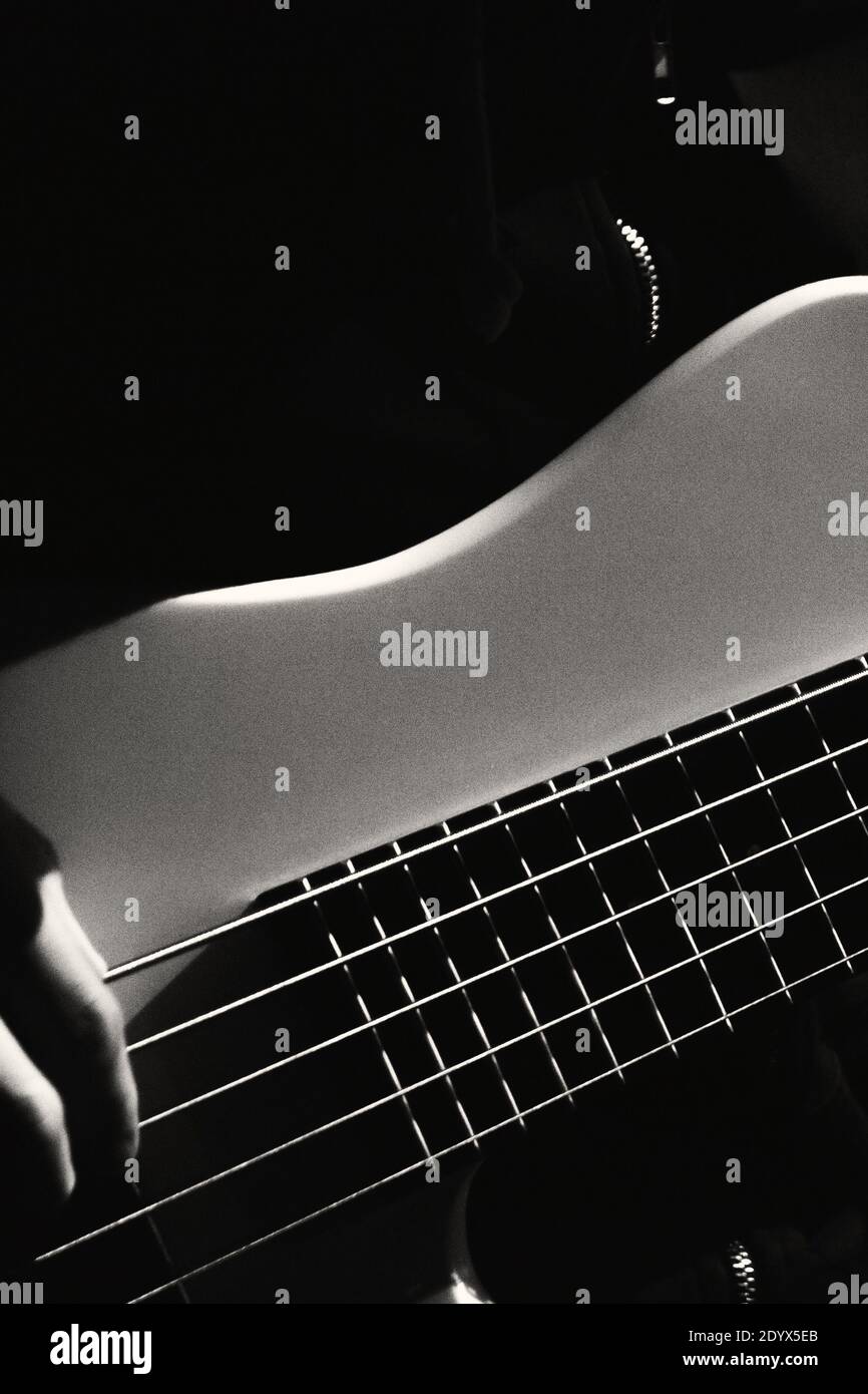 Close up view on five string bass guitar and fingers of musician lit by ...