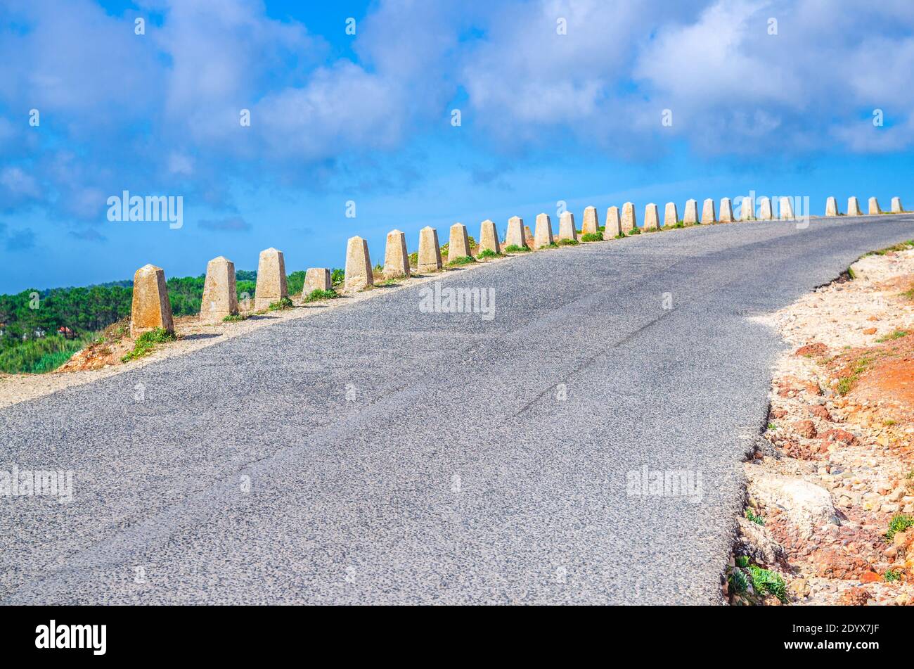 Asphalt road with stone guard barrier fence leading forward and right ...