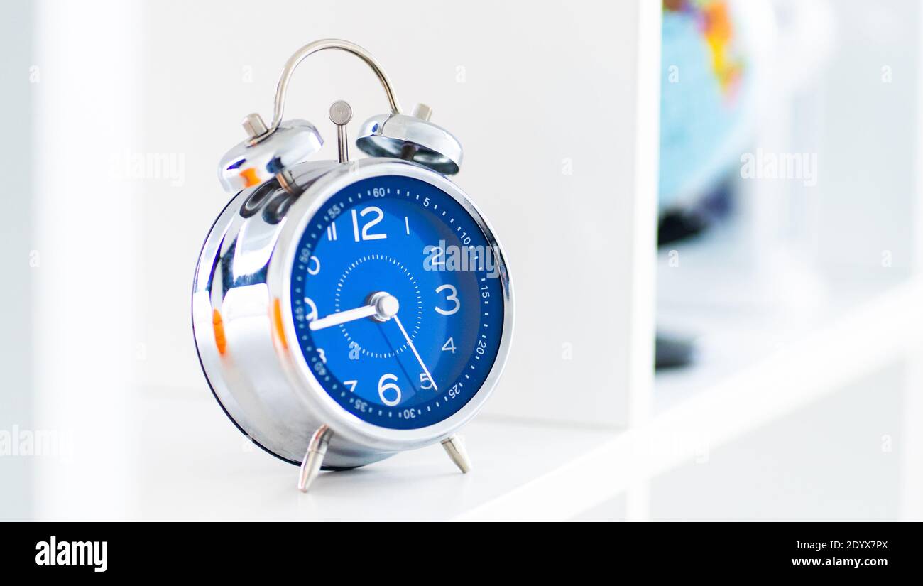 Analog alarm clock with blue clock face in white interior, close up ...