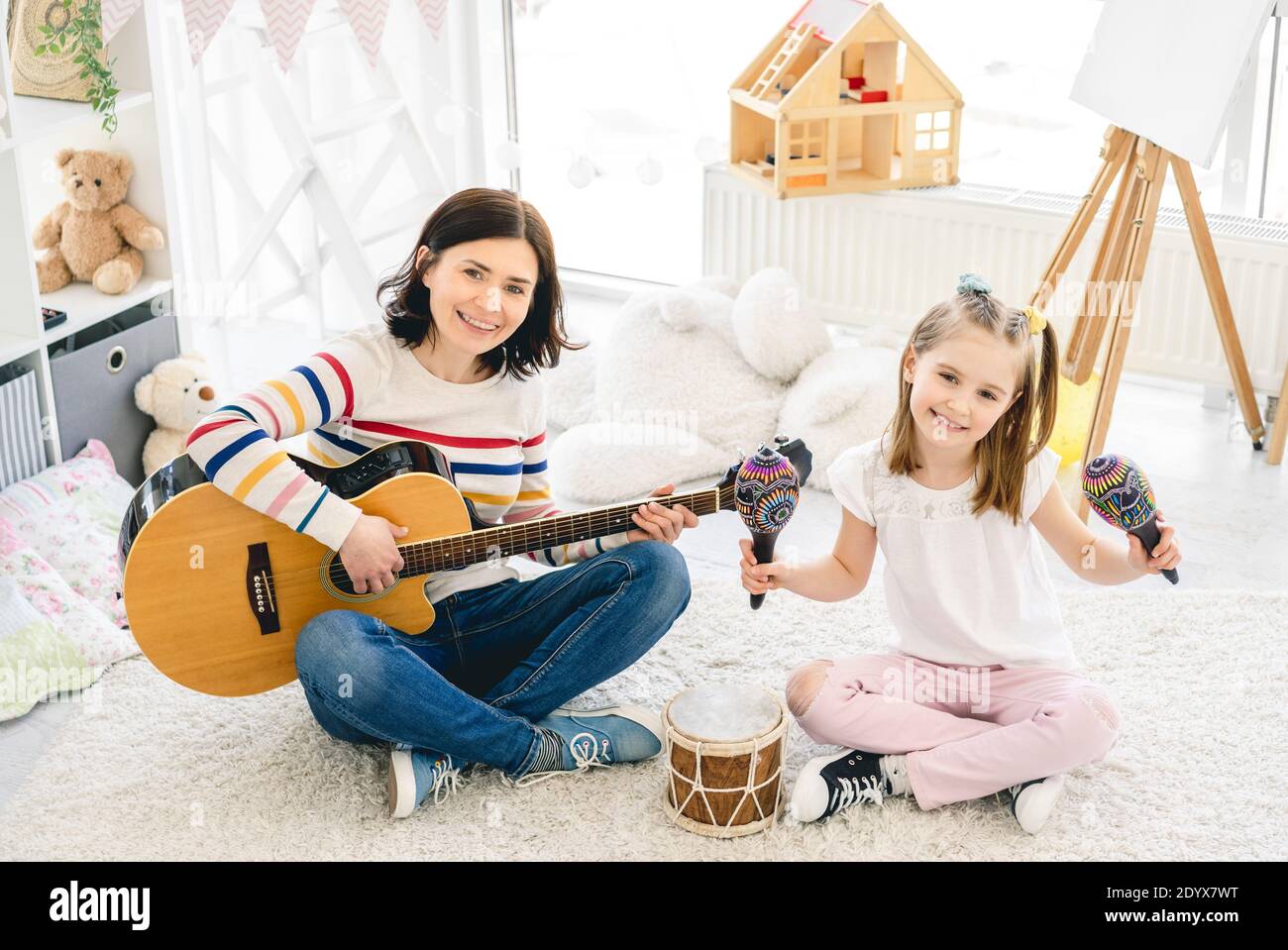 Nice little girl and mother playing musical instruments in kids room ...
