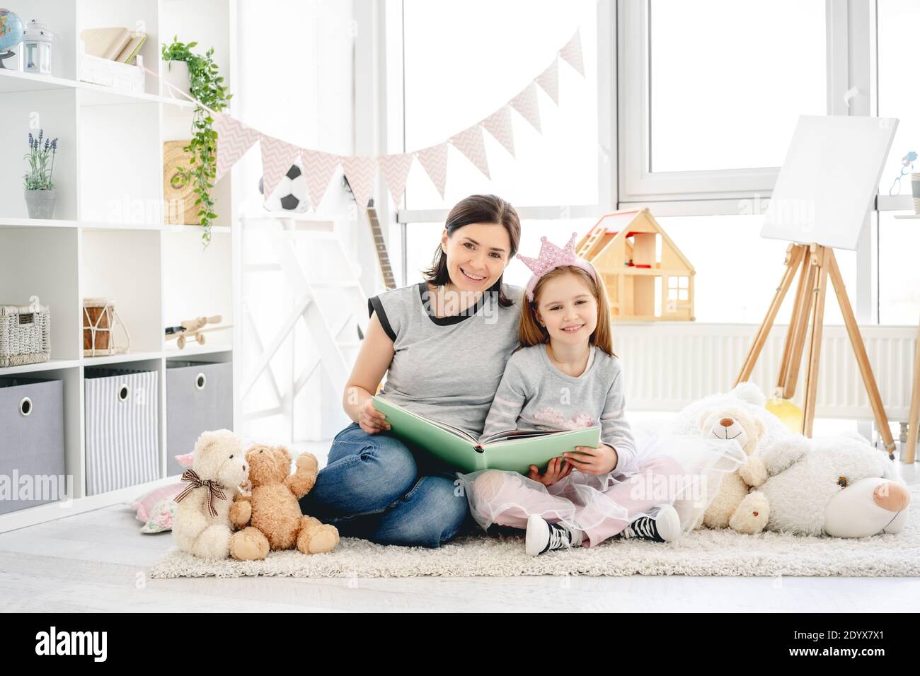 Beautiful mother and daughter reading book sitting on floor in kids ...