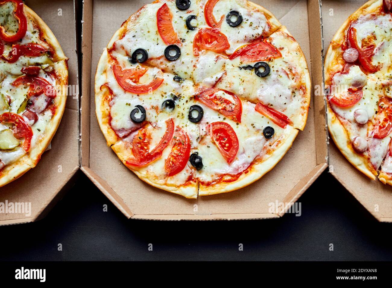 Open boxes with hot tasty italian sliced three pizzas on black ...
