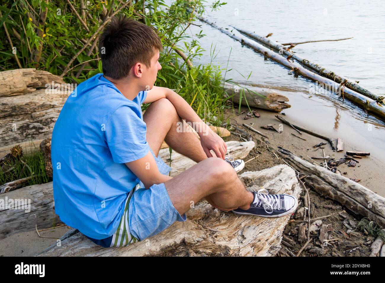 Pensive Young Man sit on the Log near the Water Stock Photo - Alamy