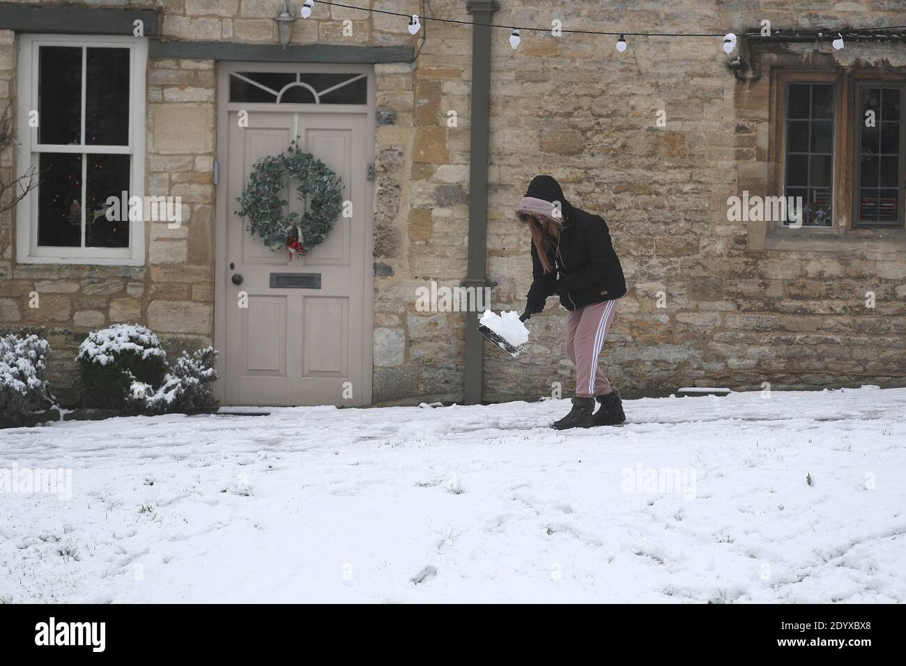 A woman clears snow from pathways in Burford, West Oxfordshire Stock ...