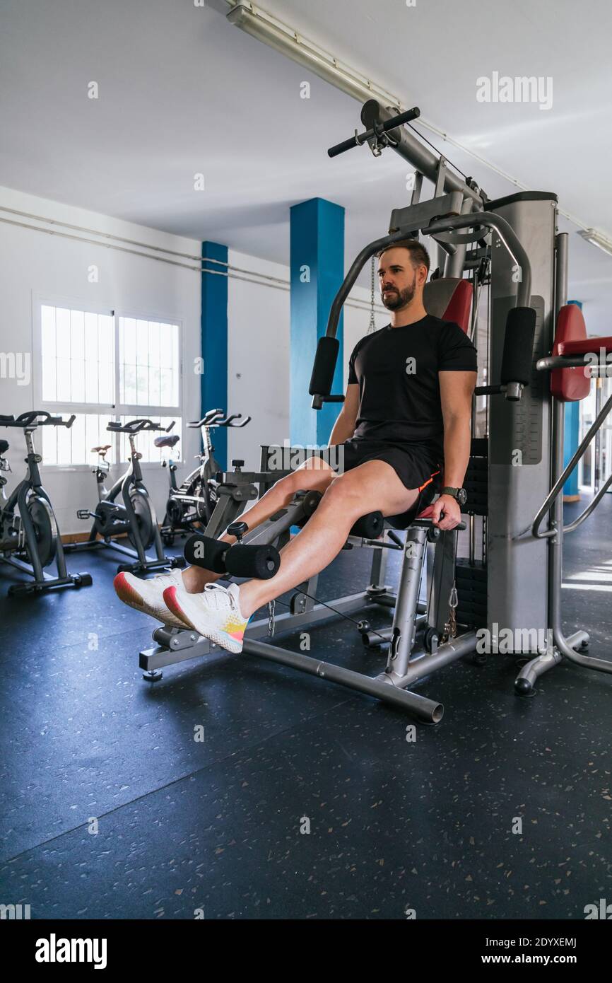 Handsome man doing leg exercises in a gym. Focus on him. Vertical Stock ...