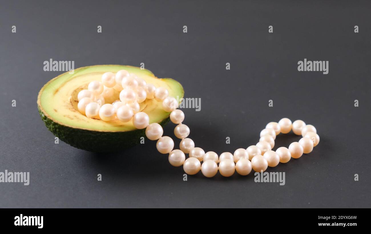 half an avocado with pearls on a black background. surrealism ...
