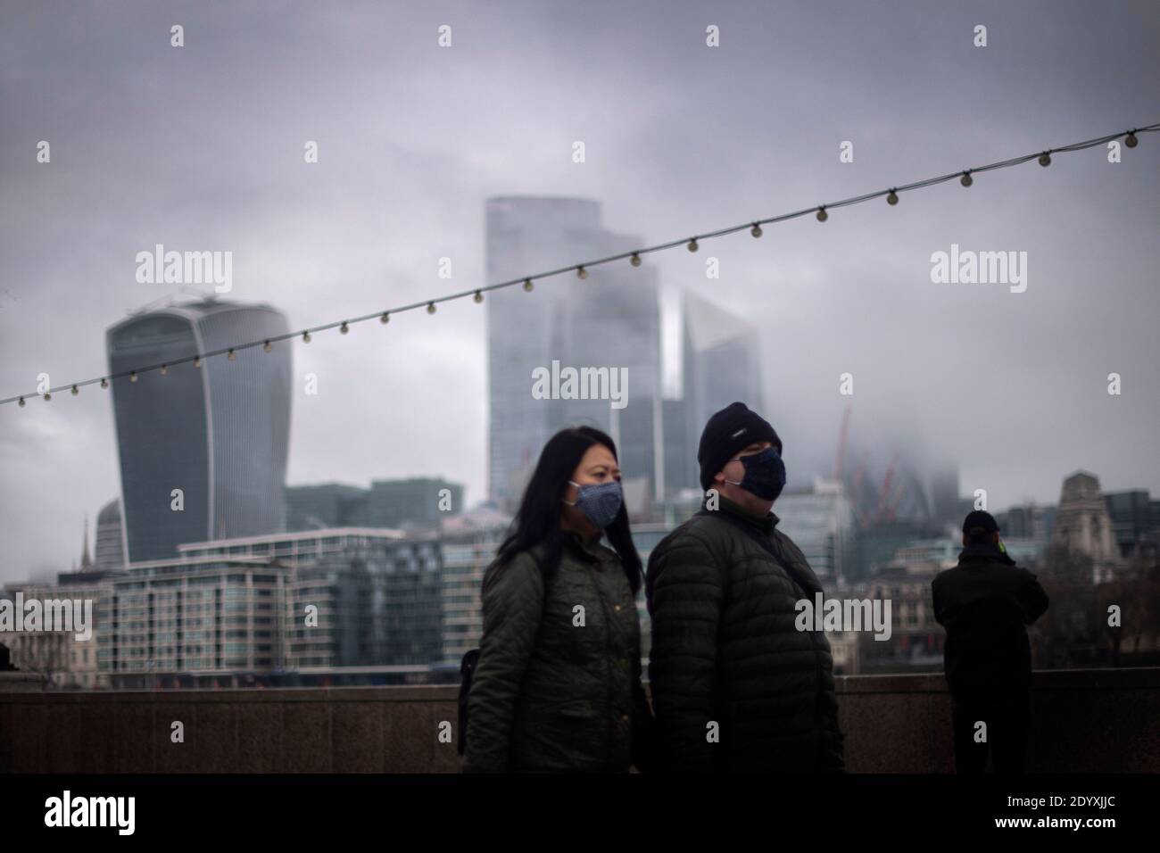 A couple wearing face masks walk past a view of the City of London ...