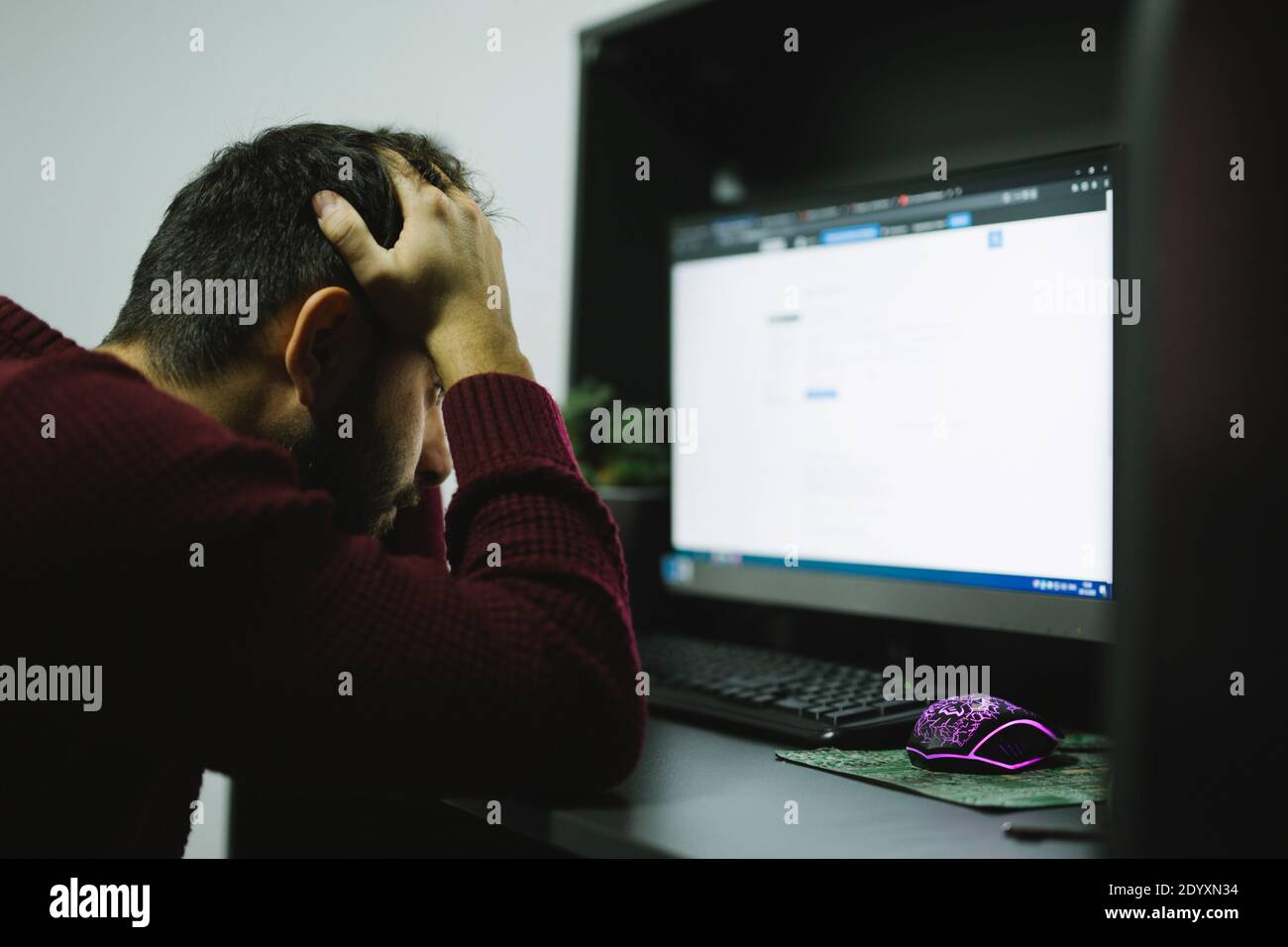 A tired young man sitting in an office in front of a computer holding ...