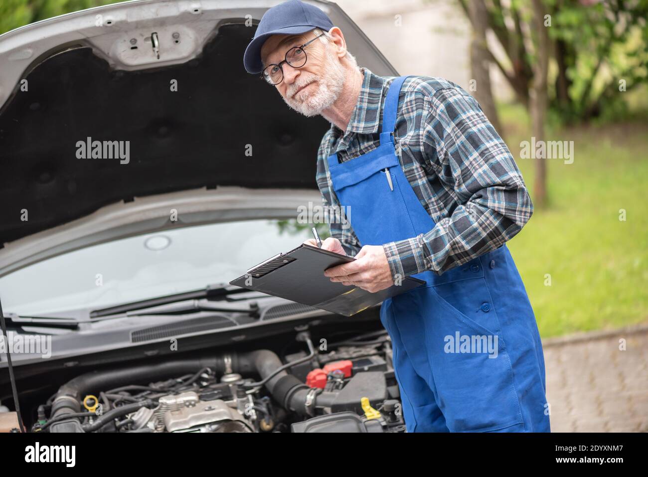 Car mechanic checking a car engine and writing on clipboard Stock Photo ...