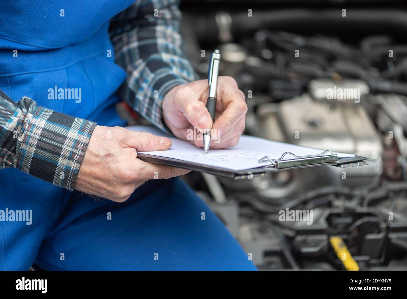 Car mechanic checking a car engine and writing on clipboard Stock Photo ...