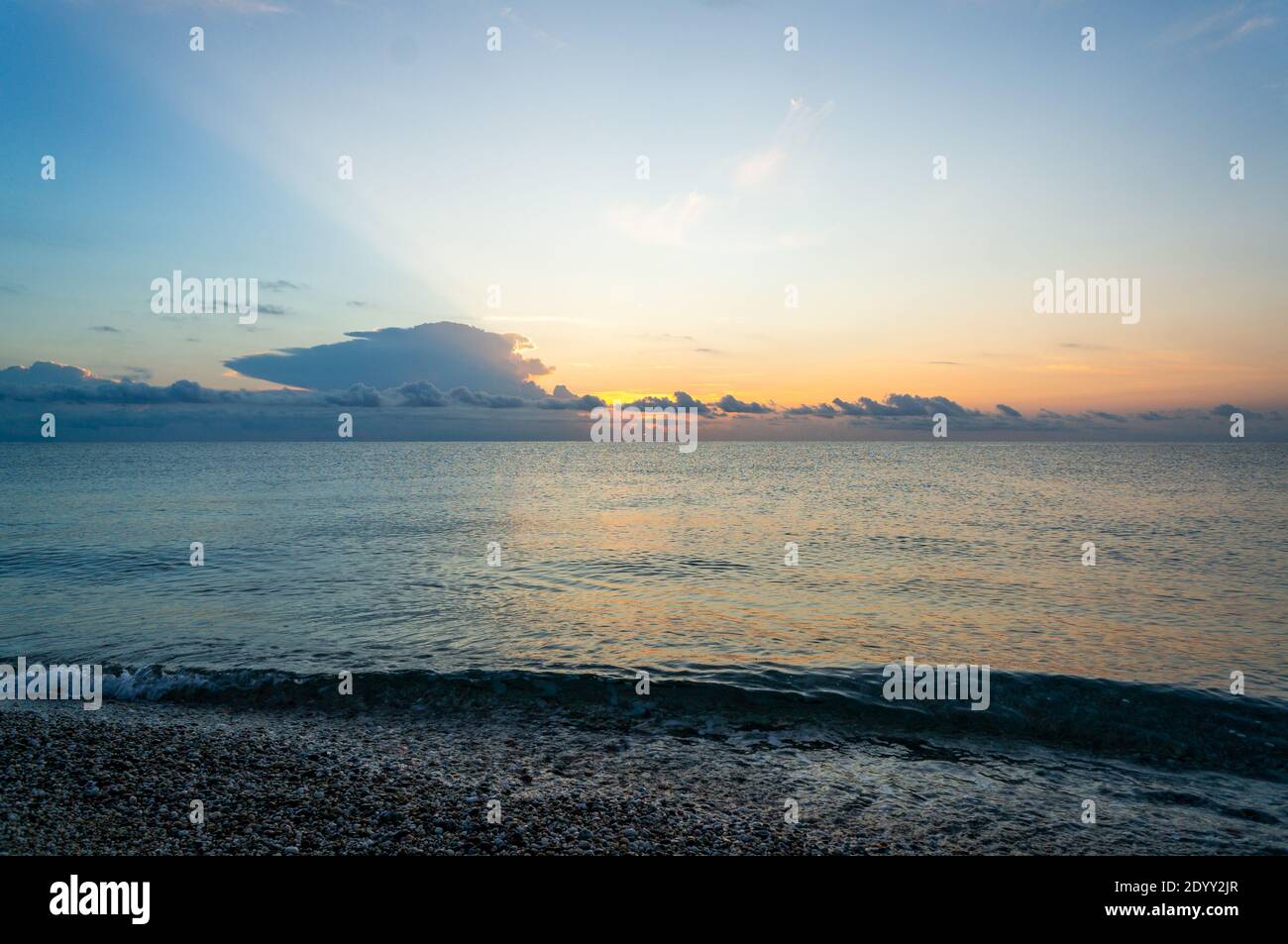 Sun rising over the sea. Small waves and beach in the forground, clouds ...