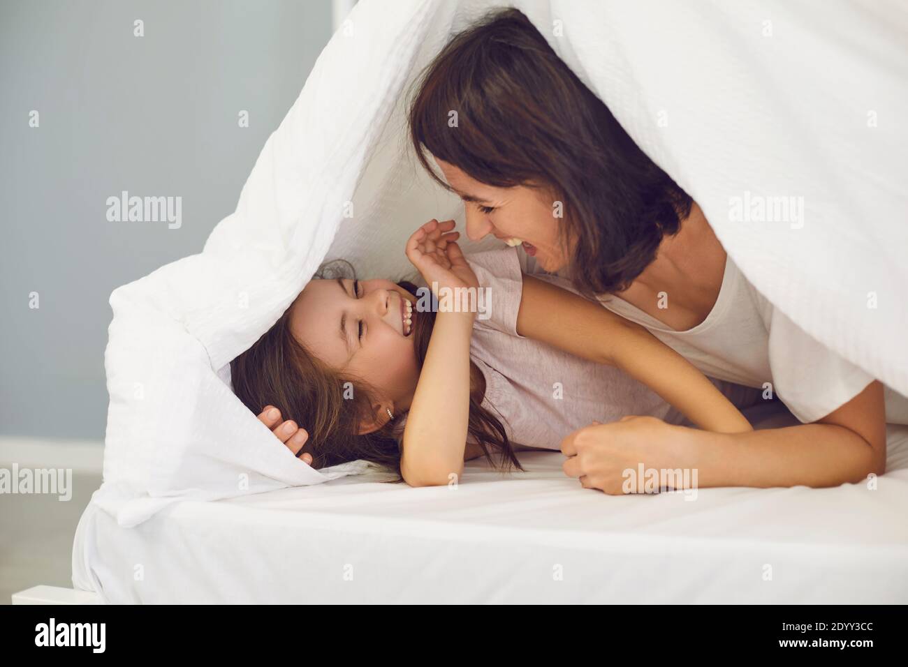 Mother and her preschool daughter have fun playing together on the bed ...