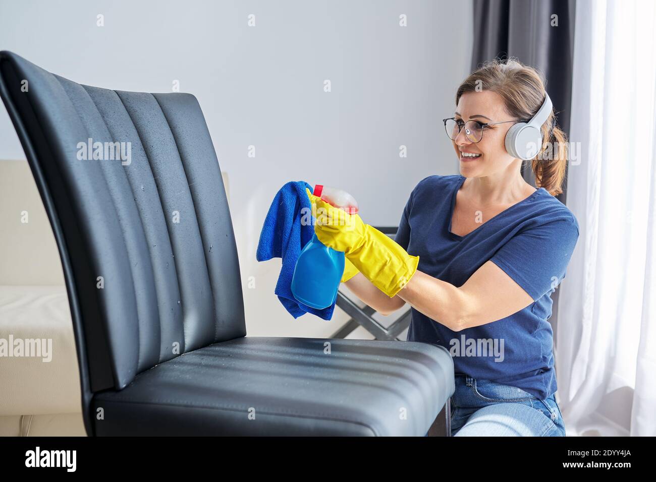 Home cleaning, woman in headphones and gloves with rag washing leather ...