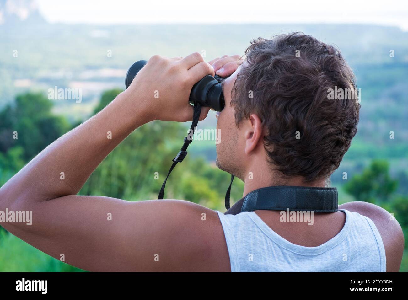 A young man looks through binoculars from the top on the background of ...