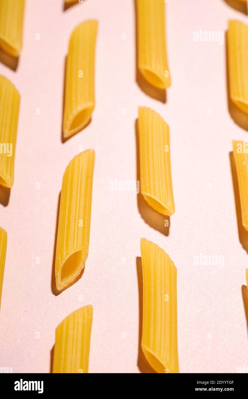 Italian pasta, raw penne tube macaroni pattern on bright pink cream ...