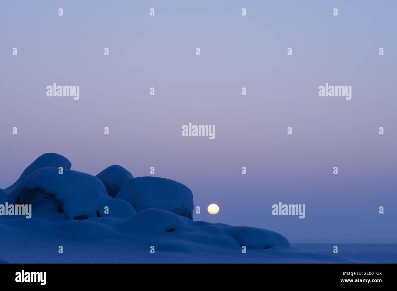 Winter landscape at dusk. Sun setting behind snow covered boulders ...