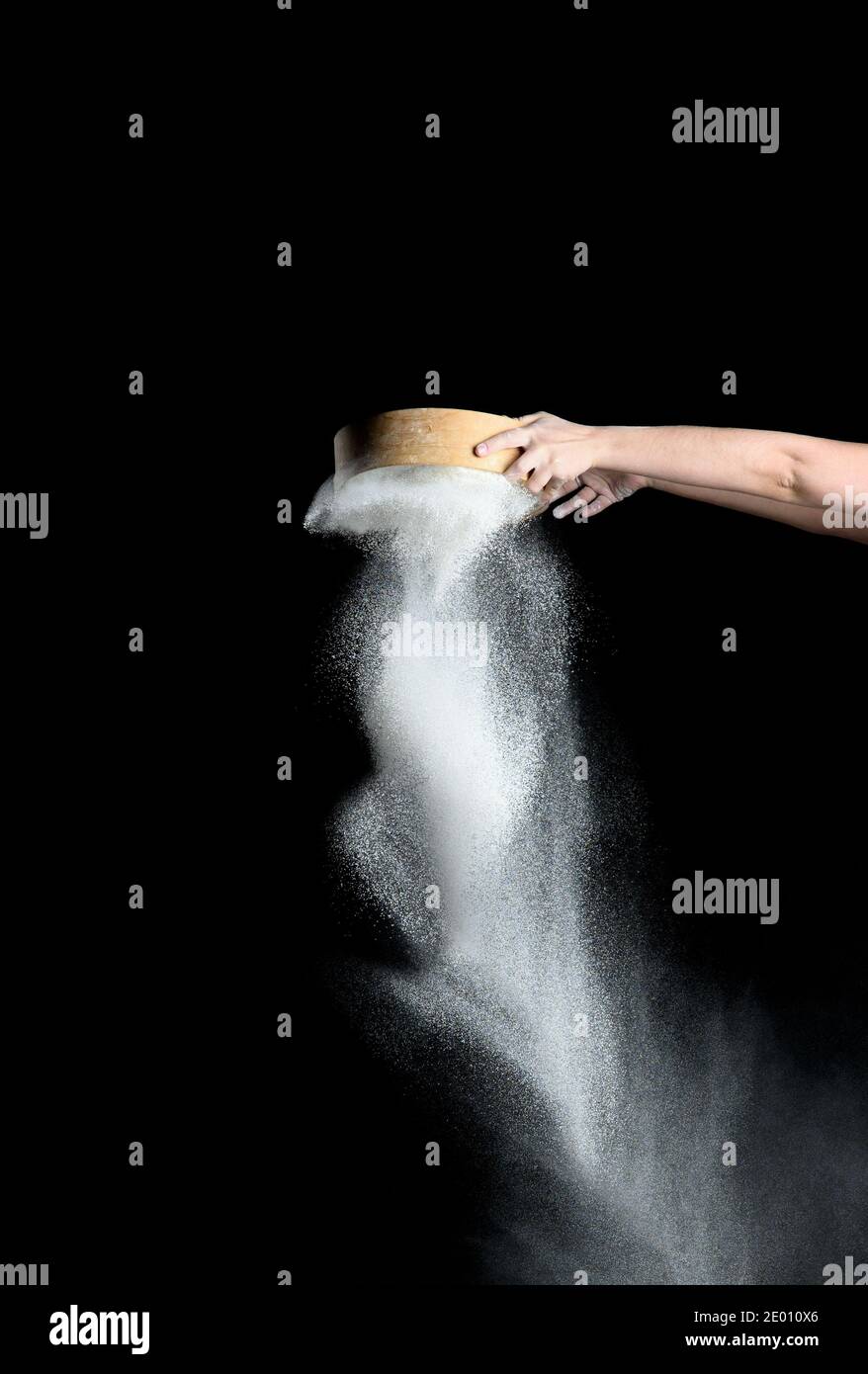 female hand sifts white wheat flour through a round wooden sieve on a ...