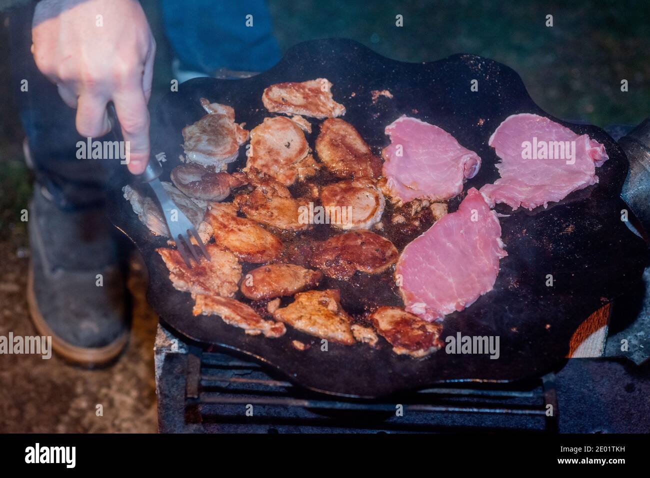 Fresh cut bacon being cooked over a campfire. The meat is fried in a ...