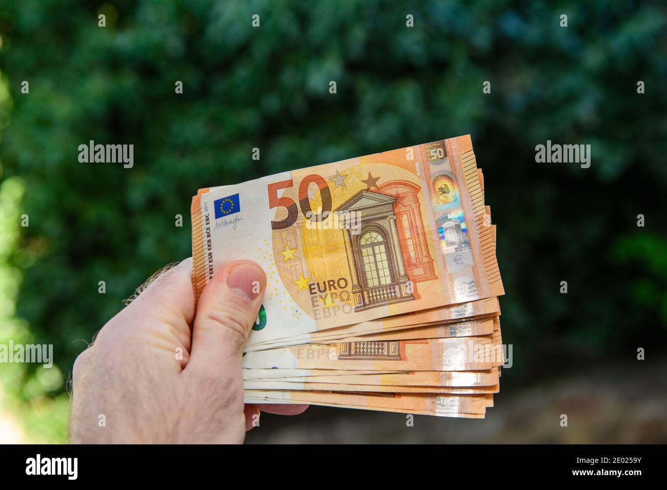 Male hand holding multiple 50 euro bills against green background Stock ...