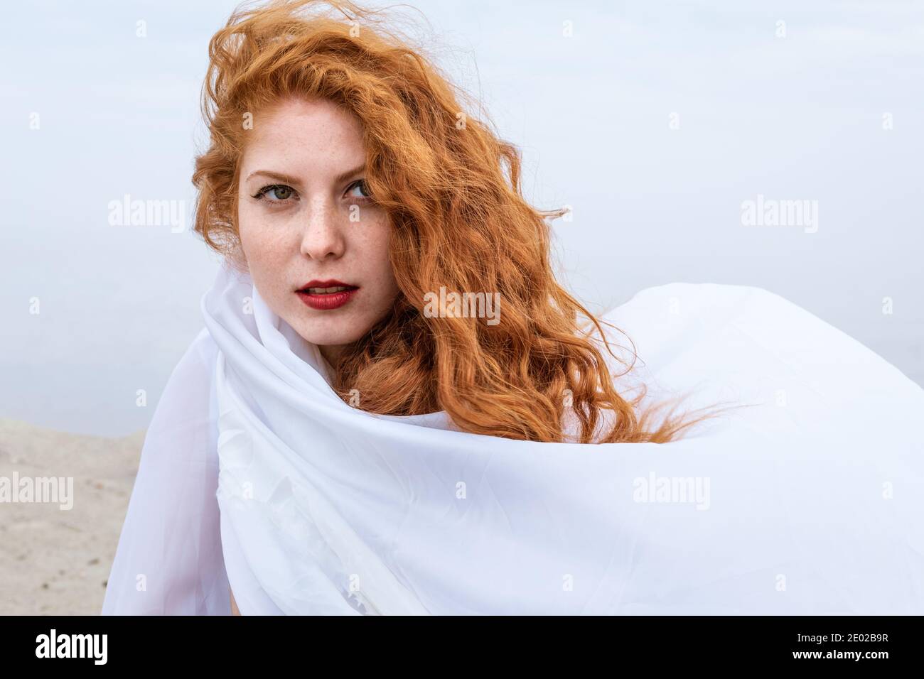A young red-haired woman is wrapped in a white sheet outdoors. Well ...