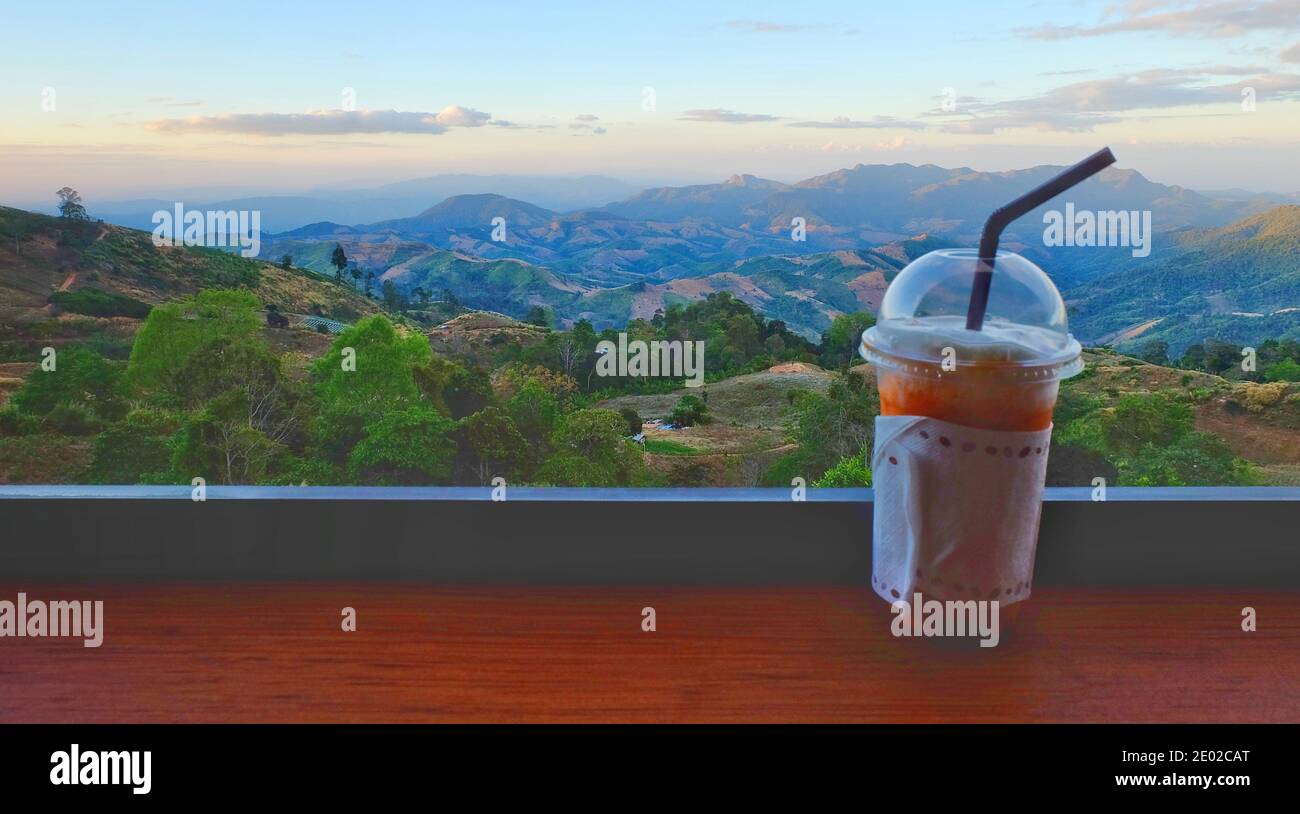 A cold cup of ice tea on a table overlooking a beautiful mountain range ...