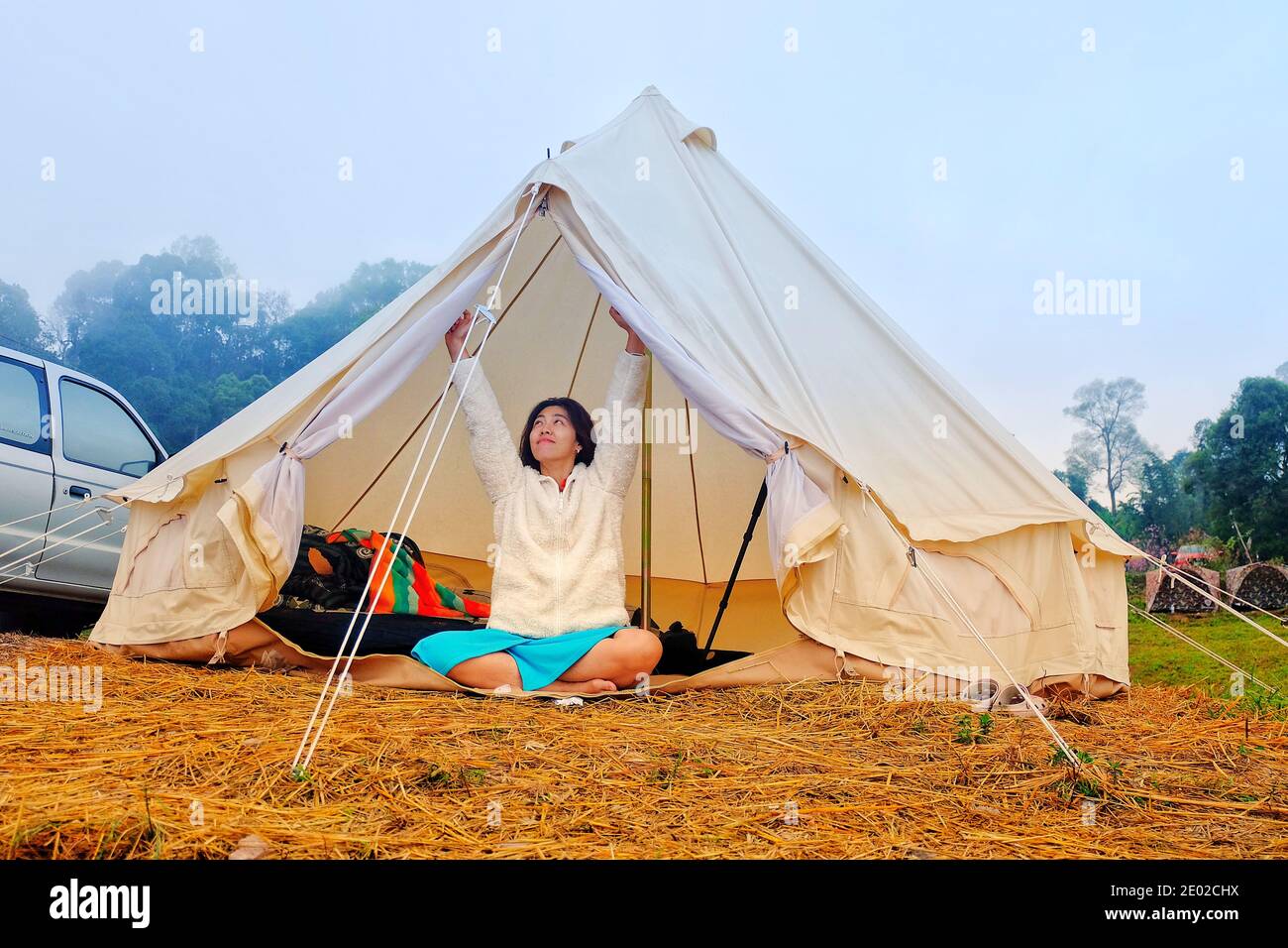 A young woman sitting peacefully inside her white tent in the morning ...