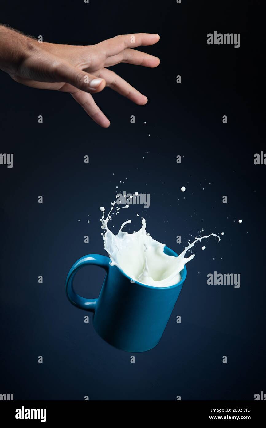 Glass of milk with splash falling from the hand on dark blue background ...