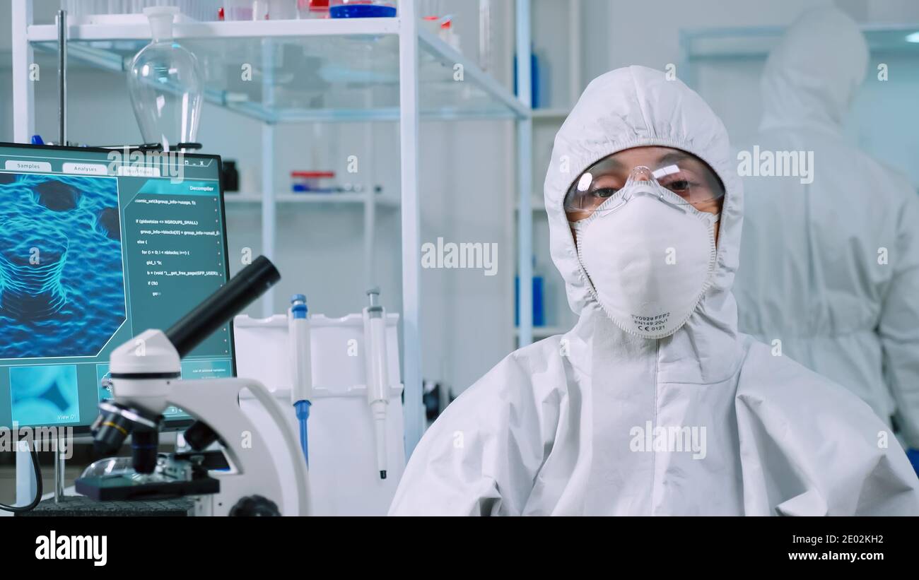 Microbiologist sitting in laboratory wearing ppe suit looking at camera ...