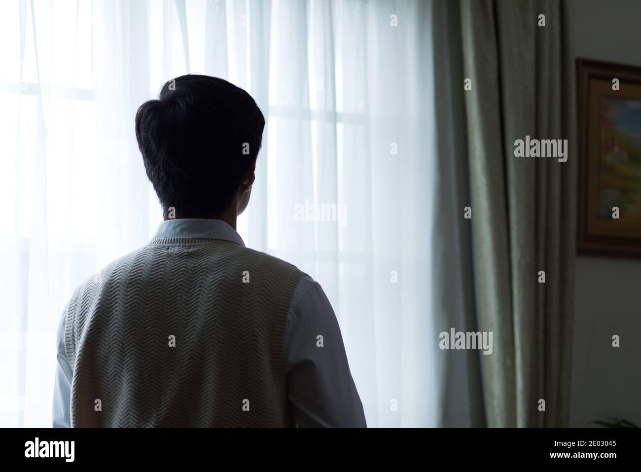 Side view of a young thinking businessman standing by an indoor window ...