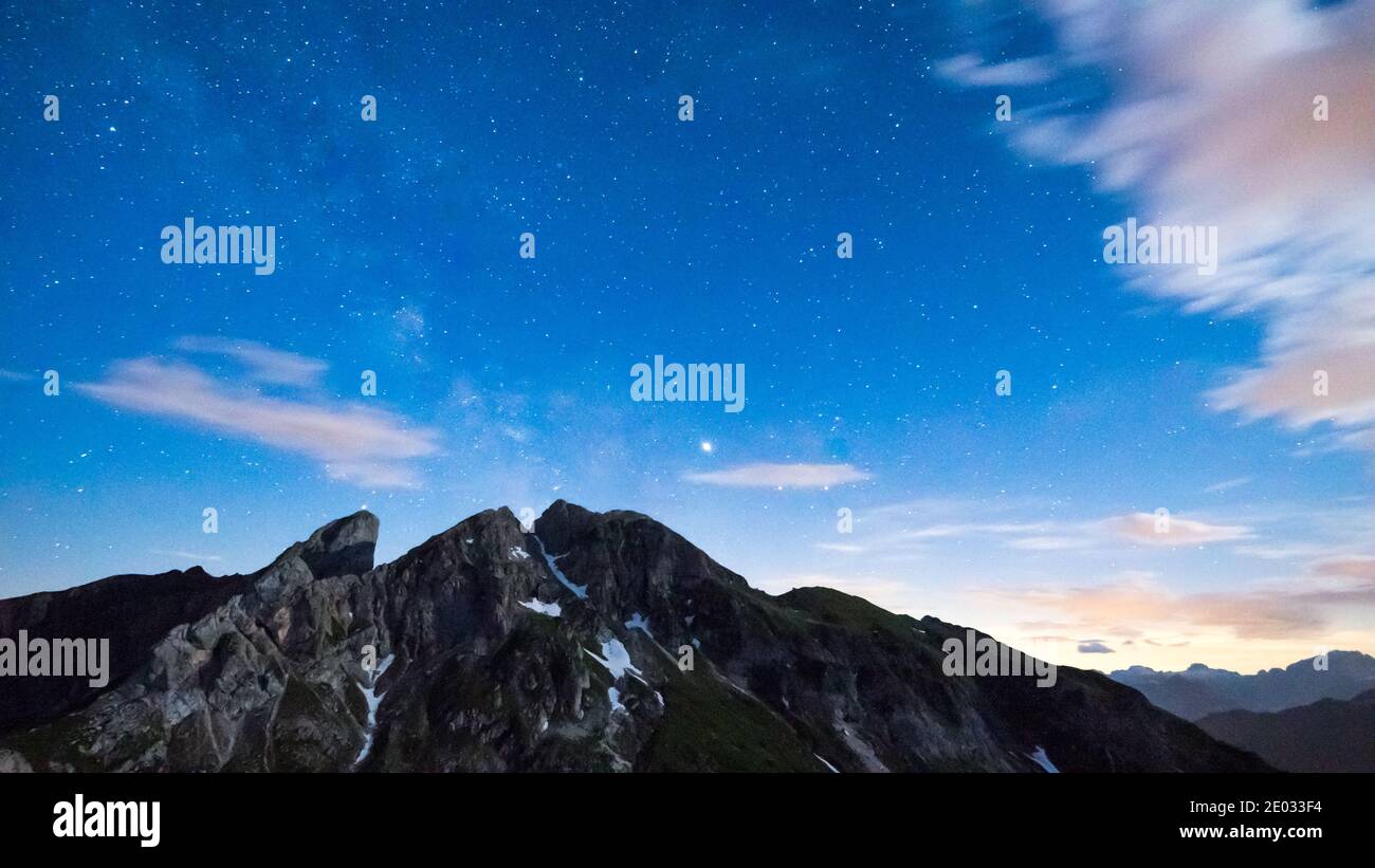 Stars in the night sky and clouds over alpine peaks. Low angle view ...