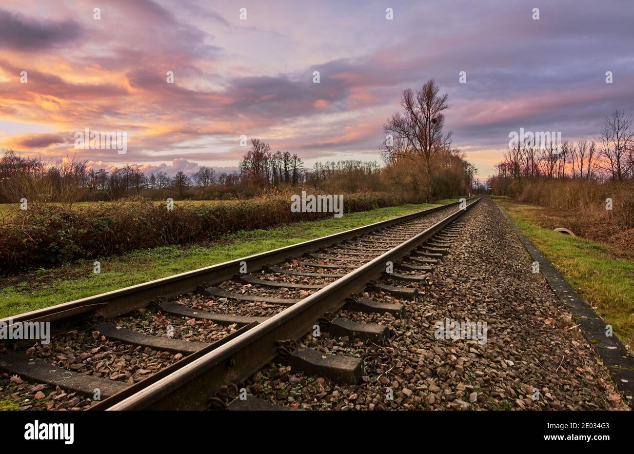 Diagonal railway tracks in rural scene leading into distant colorful ...