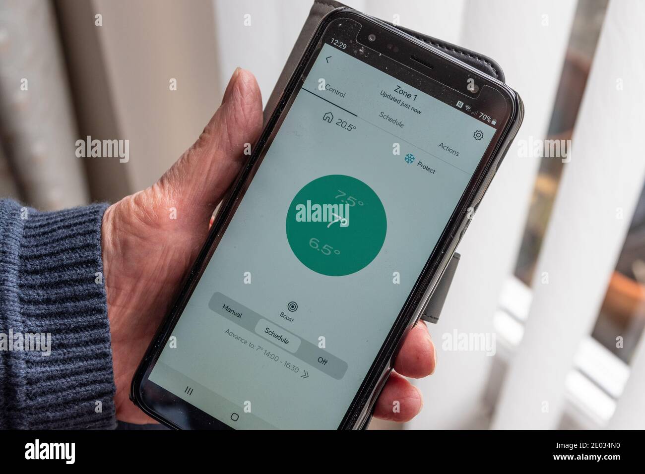 Woman using a Hive app on a smartphone to remotely control her central ...