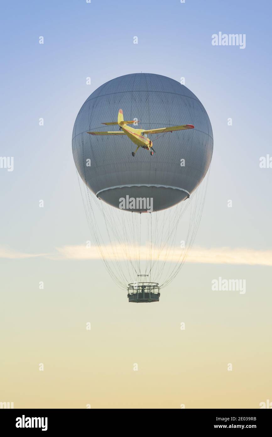 Helium balloon and a yellow aircraft seen against colorful sky at dusk ...